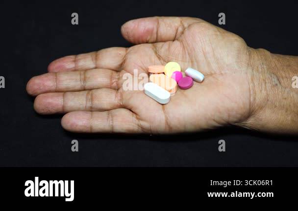 colorful medicine tablets at old age human hand on black background at ...