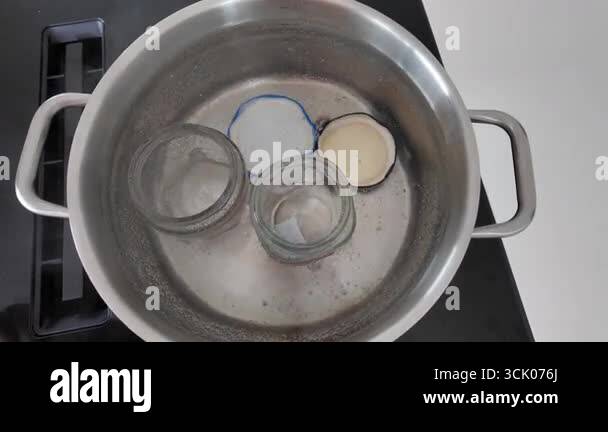 Glass jars and lids being sterilized in a large pot of boiling water on ...