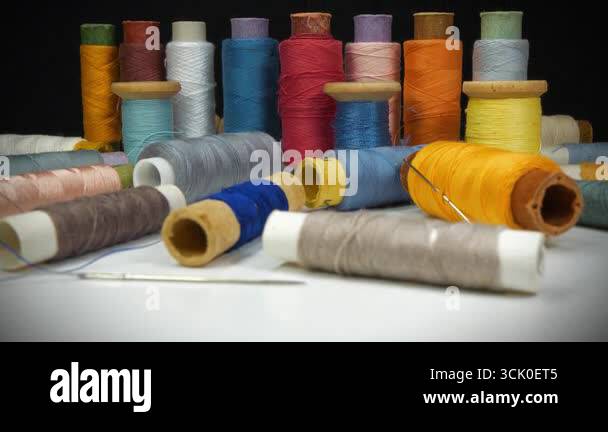 Coloured spools of thread lie on white table on black background, tilt ...