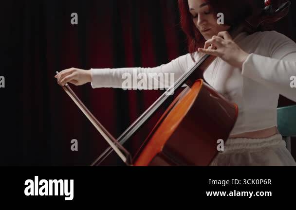 A beautiful woman sitting and playing the cello in a studio on a black ...
