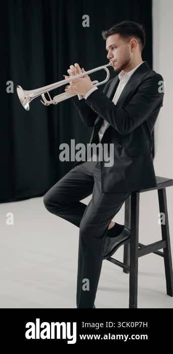 A young and handsome man dressed in a suit plays the trumpet with ...