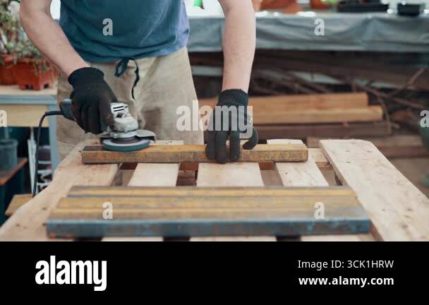 A worker is grinding rust off a steel part with an angle grinder. Close ...
