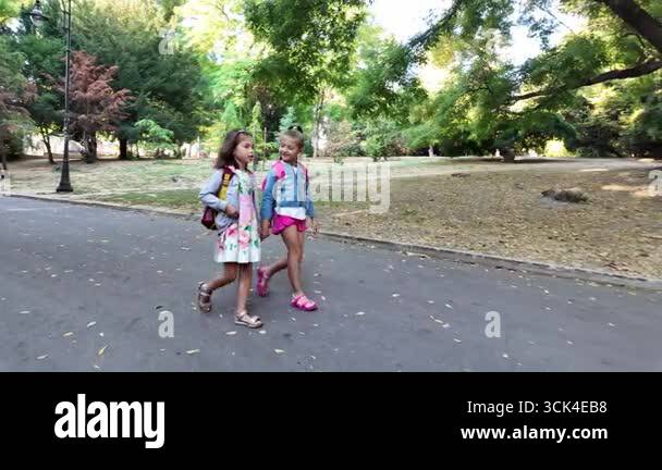Happy children. Two girls with school backpacks walking in the park ...
