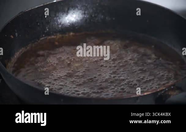 Hot oil bubbles in a black pan while frying peanuts, creating an ...