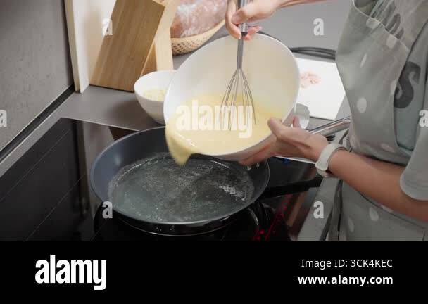 A housewife pours raw egg batter into a nonstick frying pan with melted ...