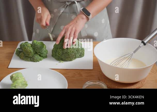 A woman is chopping fresh green broccoli on a white cutting board with ...