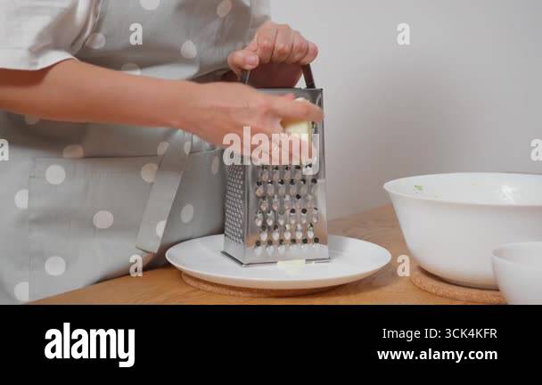 Grating a block of cheese on a metal grater. A woman is shredding ...