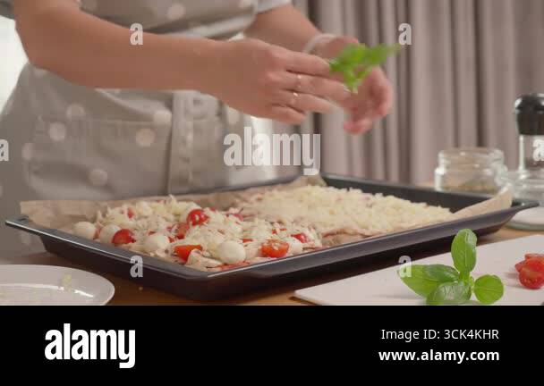 Garnishing a raw pinsa with fresh basil leaves. A cook adds the final ...