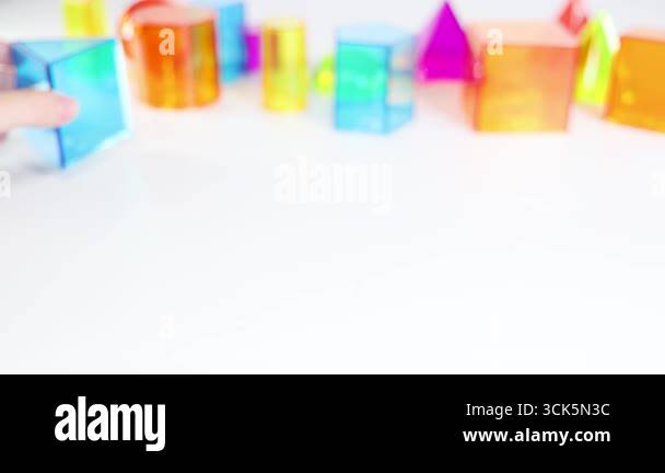 Hands manipulate colorful 3D geometric shapes on a white surface ...