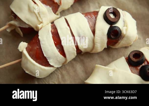 raw Halloween appetizer mummies made from sausages wrapped in puff ...