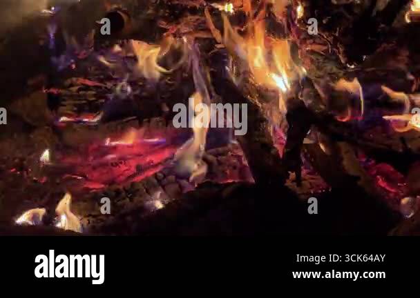 Flickering flames rise and fall among charred logs, casting warm light ...