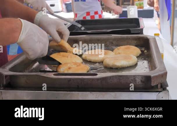 Close-up view of golden brown buns frying in oil on a metal griddle ...