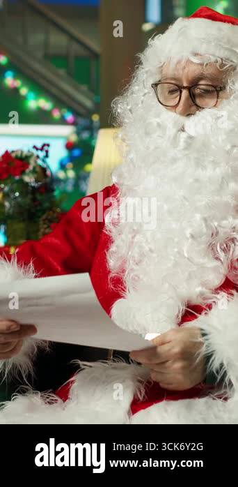 Vertical video Elderly man dressed as Santa Claus opening letter ...