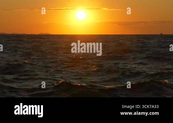 A cinematic shot of the ocean at sunset with golden reflections dancing ...