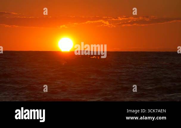 A lone motorboat cruises across the open sea with the sun setting in ...