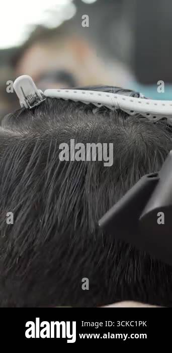 In a sleek barbershop, a dedicated barber expertly blow dries the hair ...
