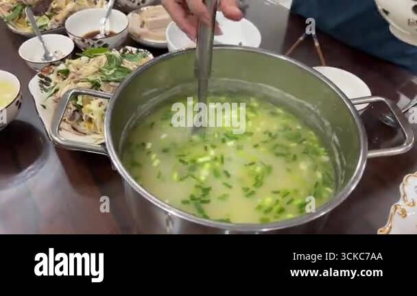 chicken soup with herbs pour into a plate from a saucepan chef hand ...