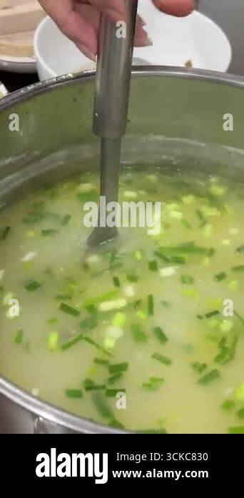 chicken soup with herbs pour into a plate from a saucepan chef hand ...