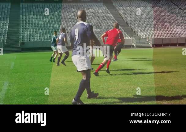 Red-jerseyed player launching rugby ball on grass pitch, navy #9 sprinting and catching under ...