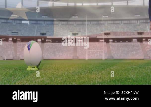 Athlete running planting foot beside tee kicking white green rugby ball ...