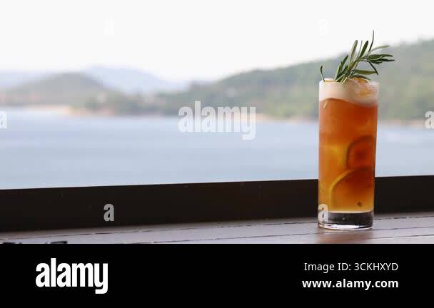 A hand picks up a cocktail from a ledge overlooking a serene seascape ...
