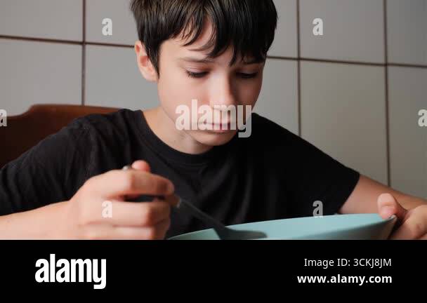 Side closeup of a teen boy lifting a spoon of cereal with milk from a ...
