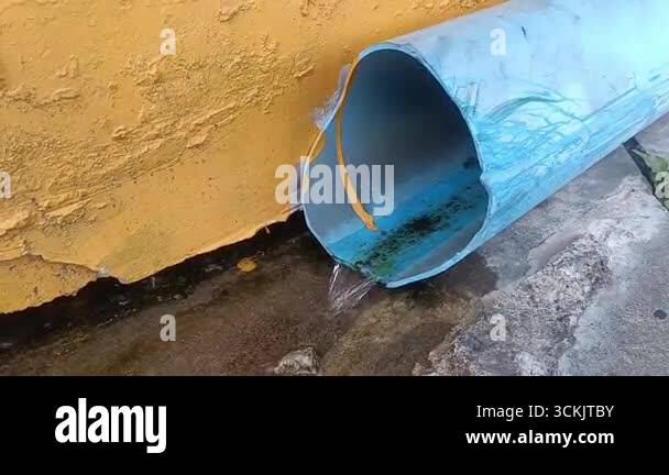 Blue drainage pipe pouring water onto concrete near yellow textured ...