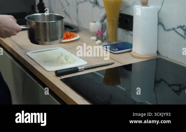 An experienced chef places a pot of water on an induction hob and cooks ...