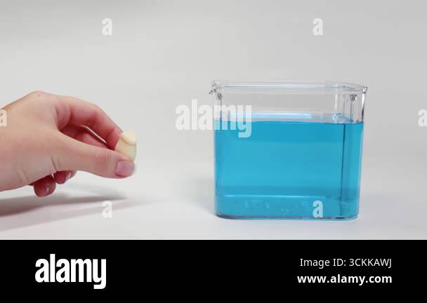 A hand drops a small object into blue liquid, observing its buoyancy ...