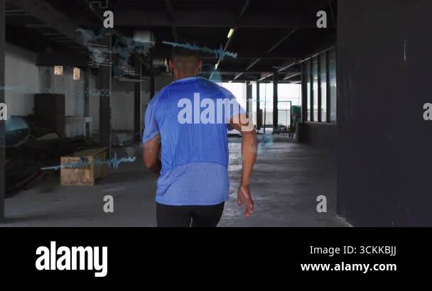 Male runner leaning forward sprinting through industrial hall, graph ...