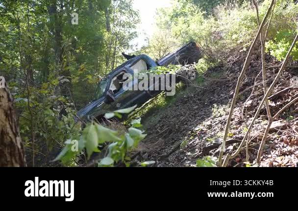 A wrecked truck sits on a steep slope in a forested area, partially ...