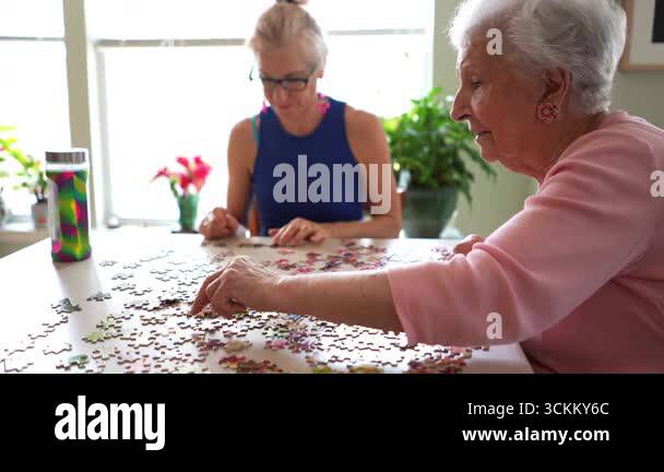 Two happy elderly mature women talking and playing with puzzle pieces ...