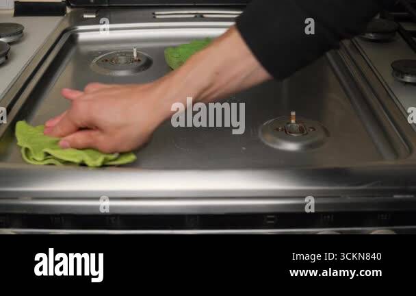 Cleaning gas stove at home. Hand wiping kitchen surface with green ...