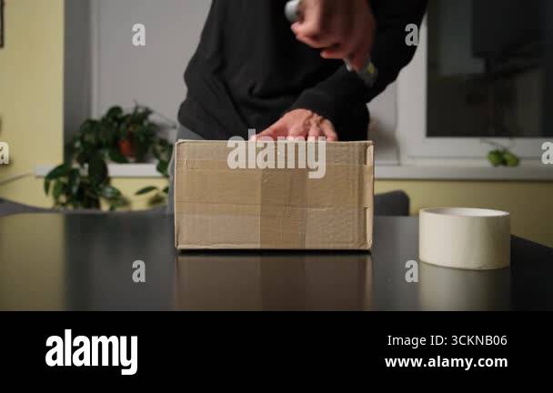 Hands unboxing parcel at home, cutting packing tape on cardboard box ...