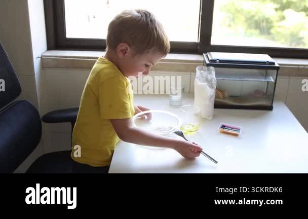 Child learning to cook, mixing ingredients in a bowl on a table in a ...