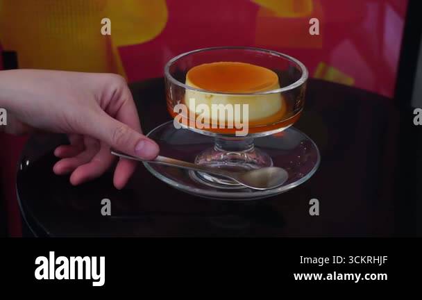 A woman's hand picks up a spoon and scoops up caramel custard pudding ...