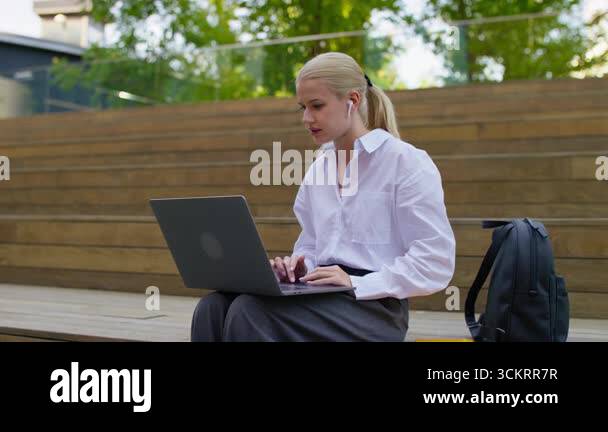 Young woman sitting outside with a laptop, holding her head in ...