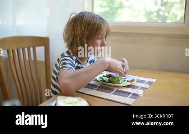 Young child eating chicken and salad at home dining table. Natural ...