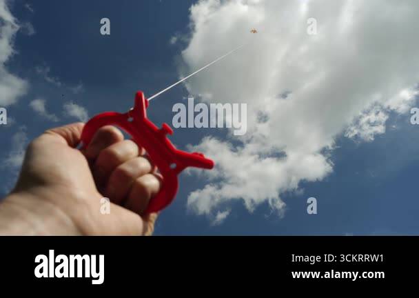 In the shot, a hand holds a kite string, framing the kite soaring amid ...