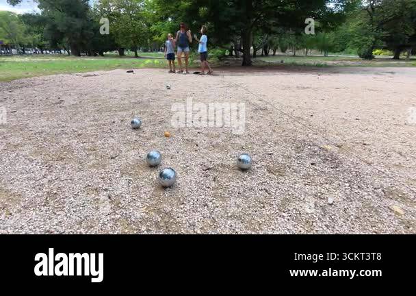Family playing petanque together in the park. Adults and children take ...