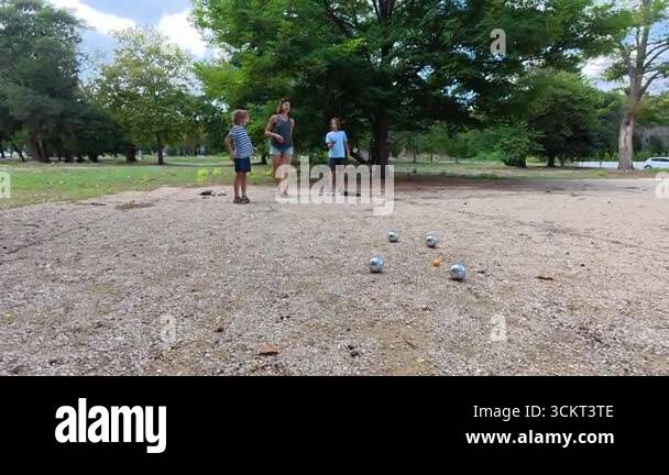 Family playing petanque together in the park. Adults and children take ...