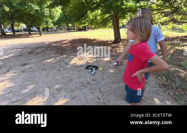 Two boys playing petanque outdoors on a sunny day. Children take turns ...