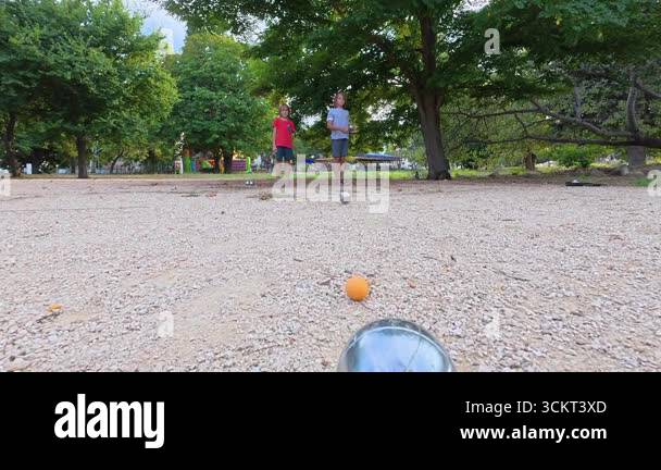 Two boys playing petanque outdoors on a sunny day. Children take turns ...