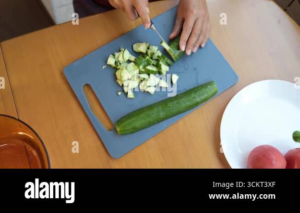 Woman slicing fresh cucumber on a cutting board in the kitchen. Close ...