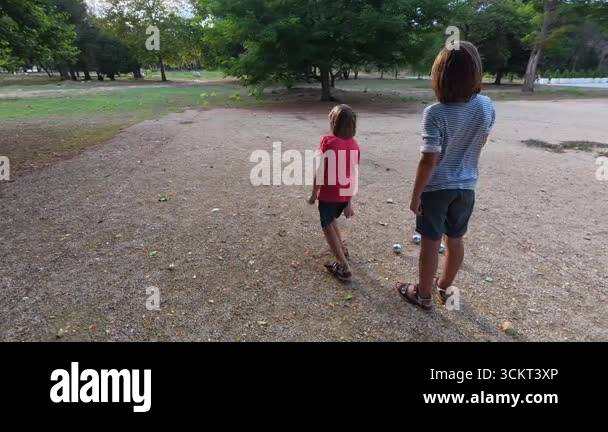 Two boys playing petanque outdoors on a sunny day. Children take turns ...