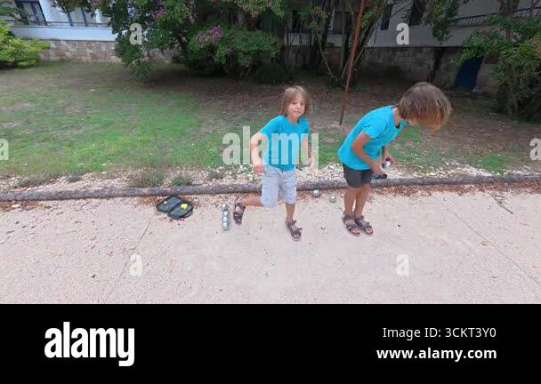Two boys playing petanque outdoors on a sunny day. Children take turns ...