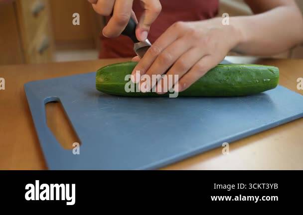 Woman slicing fresh cucumber on a cutting board in the kitchen. Close ...
