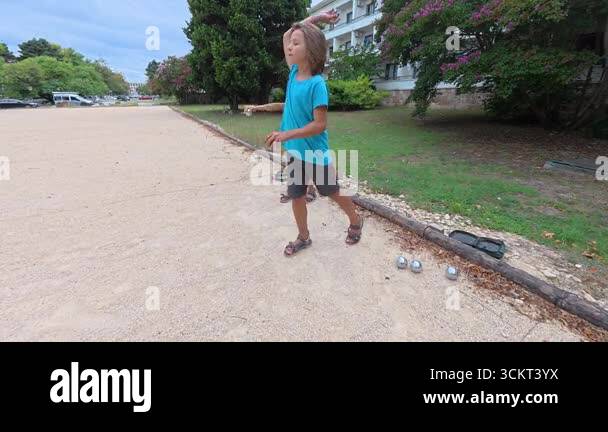 Two boys playing petanque outdoors on a sunny day. Children take turns ...