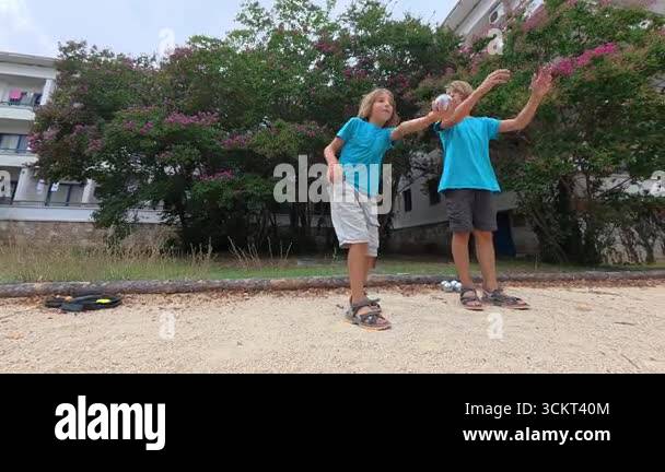 Two boys playing petanque outdoors on a sunny day. Children take turns ...