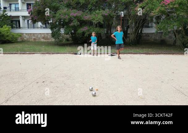 Two boys playing petanque outdoors on a sunny day. Children take turns ...